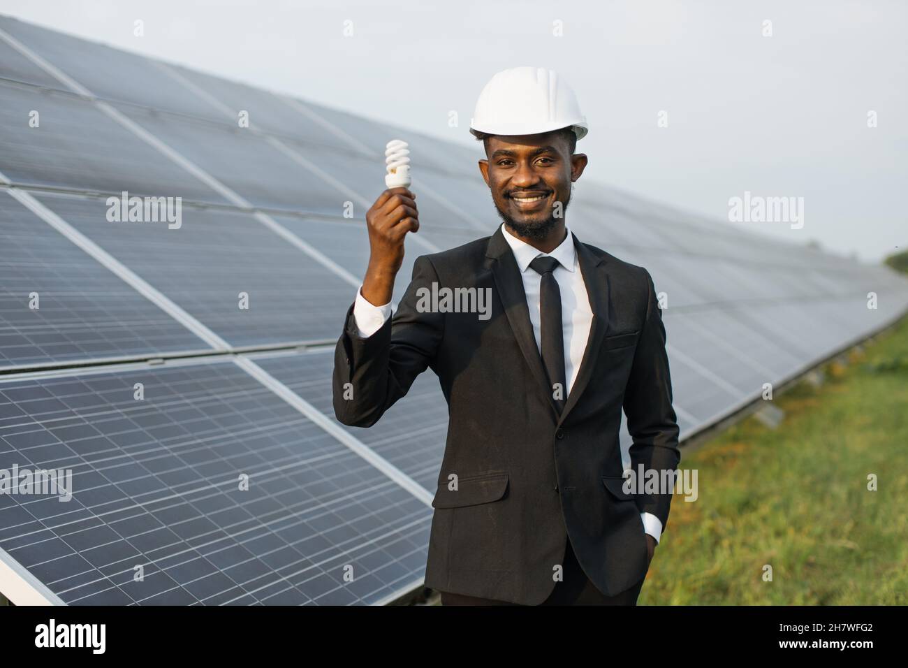 African american man with light bulb in hand standing on field with ...