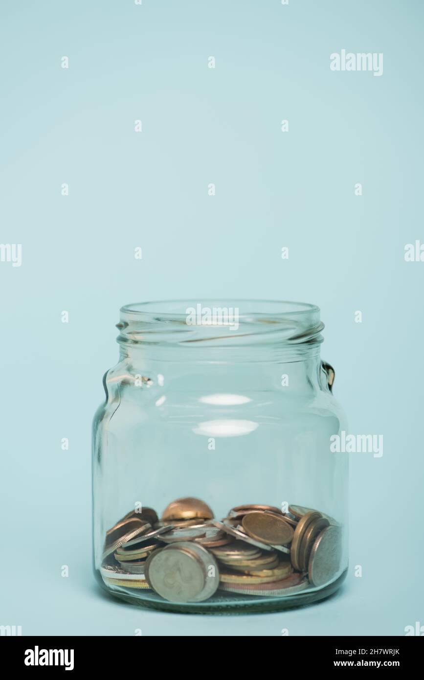 glass jar with golden and silver coins on blue background, anti ...