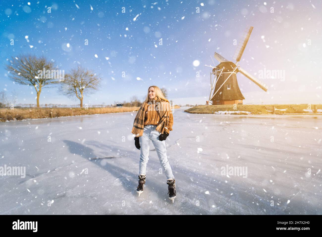 Girl having fun on ice in typical dutch landscape with windmill. Woman ...