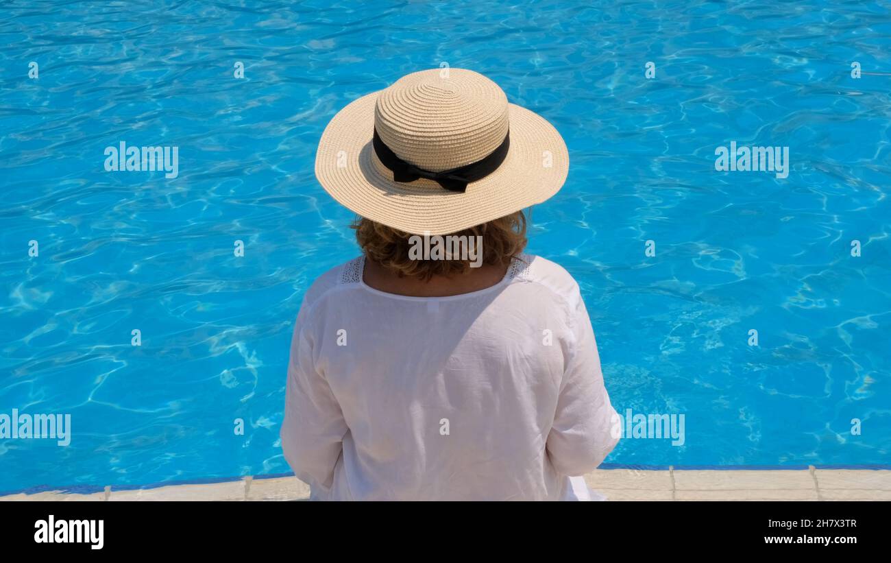 Senior woman relaxing near the hotel's blue outdoor swimming pool ...