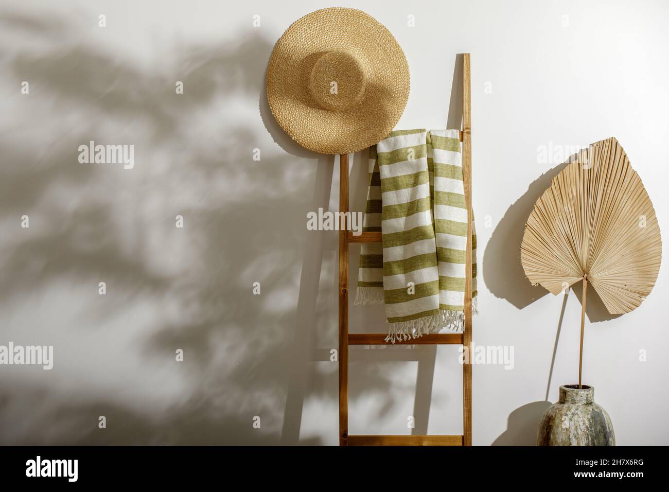 Organic linen beach towel on wood ladder, straw hat and dried palm leaf ...