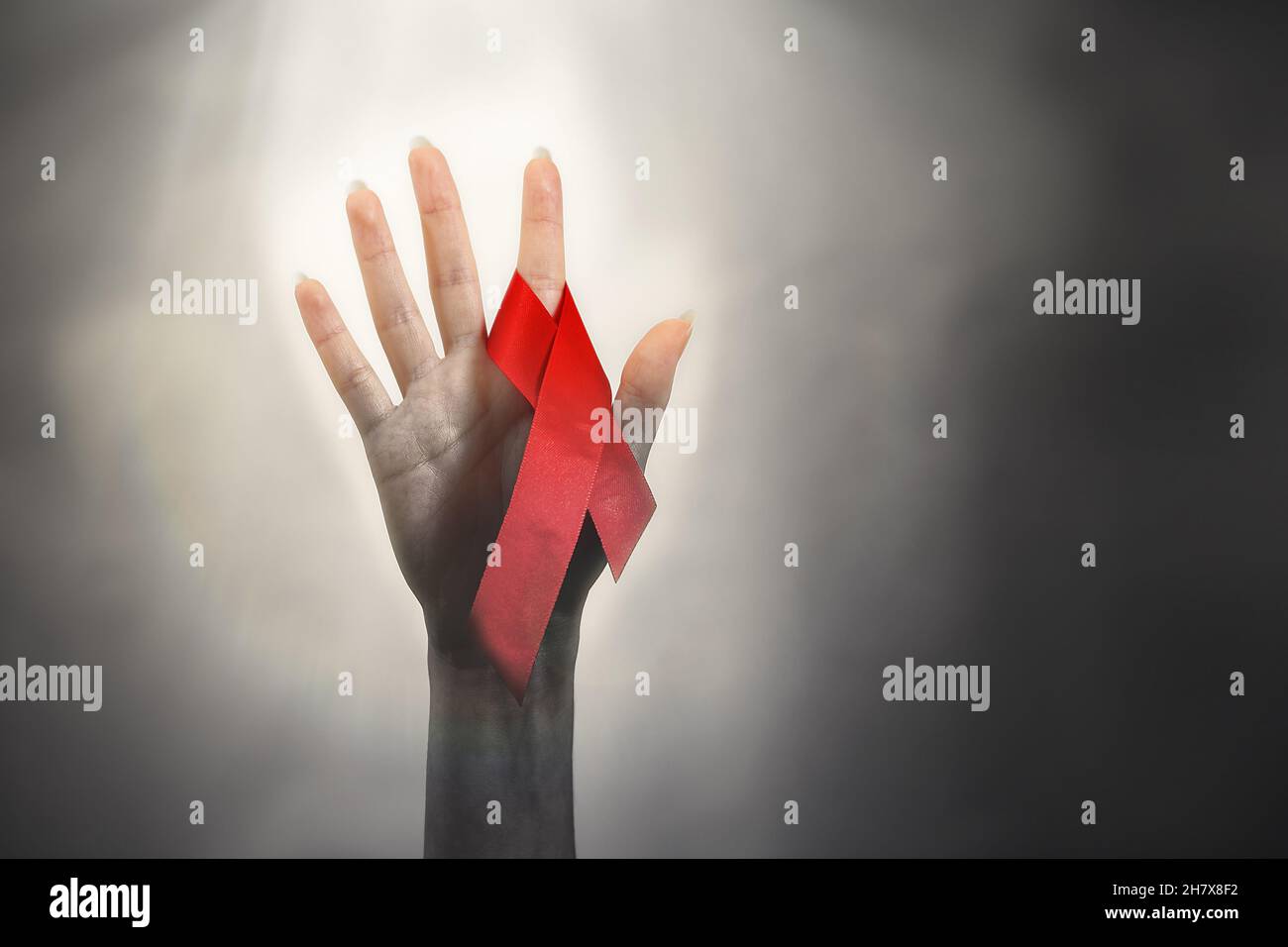A woman's hand reaches up to light, with a red ribbon on her finger ...