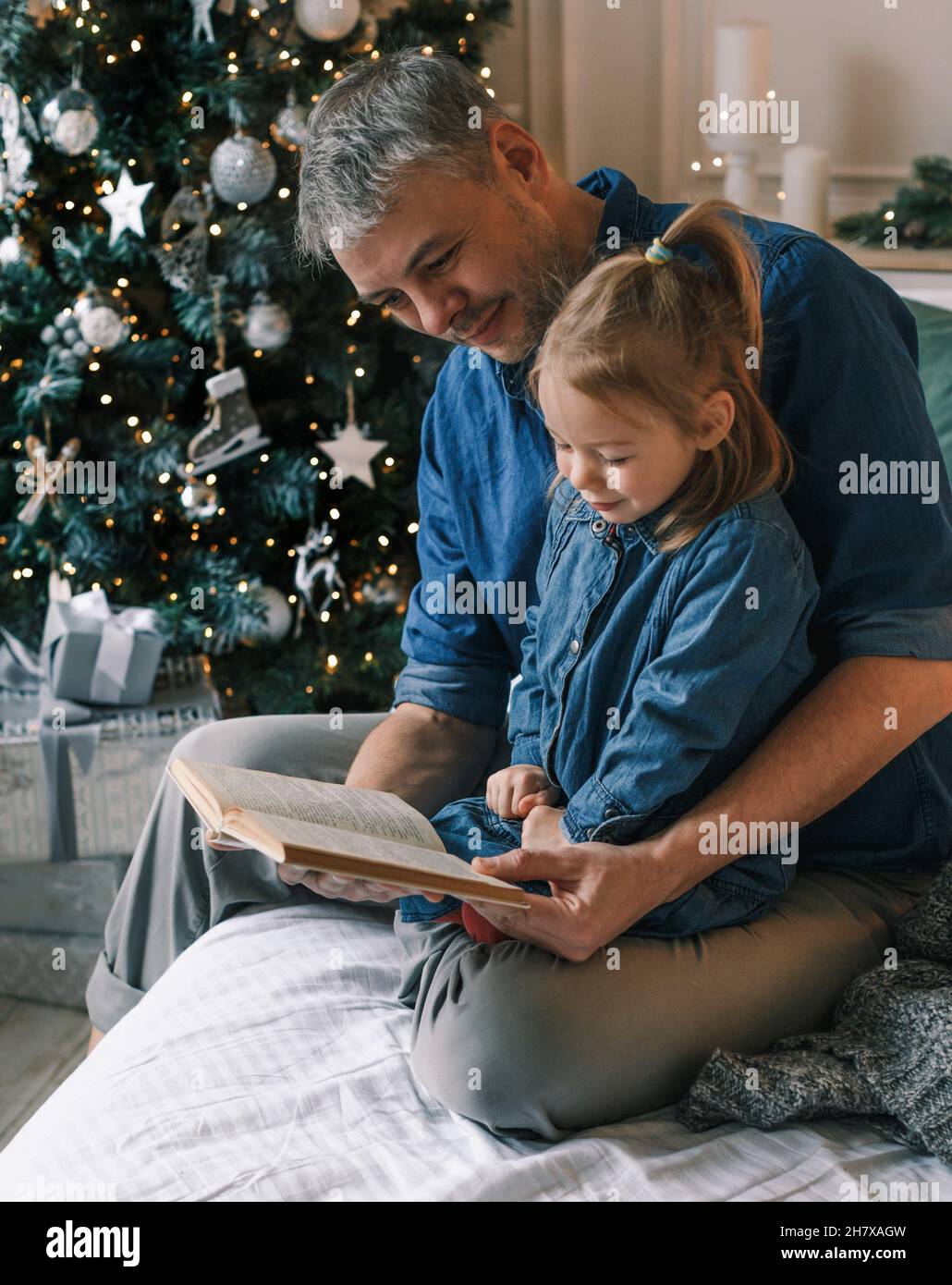 Attentive father reads a Christmas tale for a happy girl near a ...