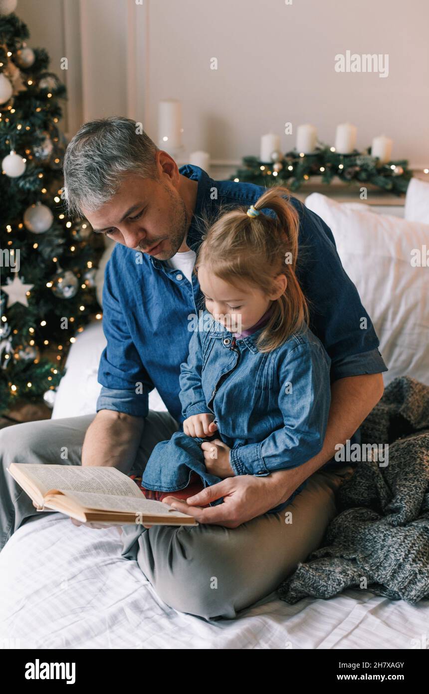 Attentive father reads a Christmas tale for a happy girl near a ...