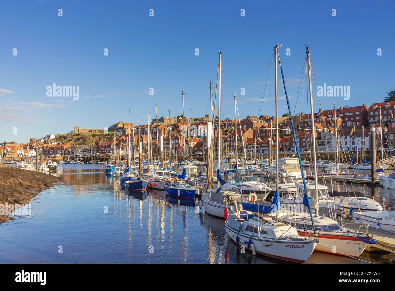 Yachts are moored to jetties in a marina. There are rows of red-brick ...