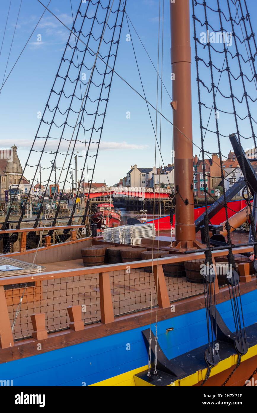 A replica of HMS Endeavour moored in harbour. Buildings and a bridge ...