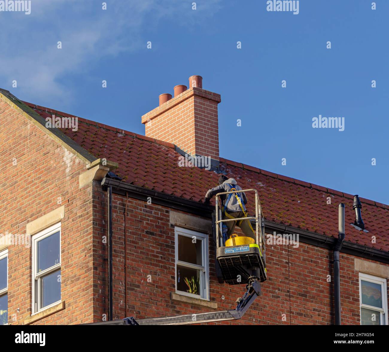 A workman in a cherrypicker repairs some guttering on a roof. The ...