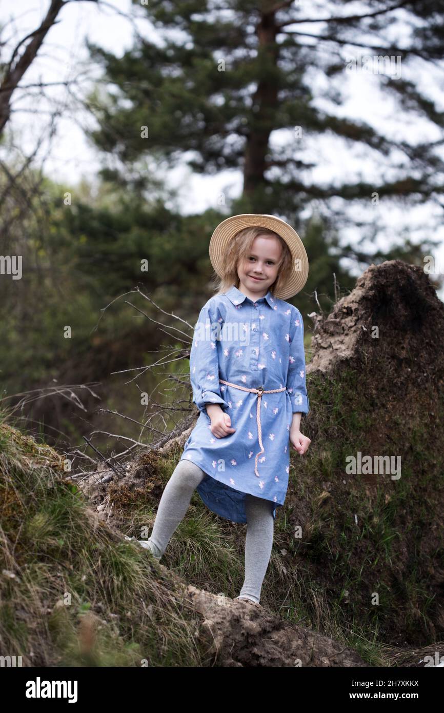 Portrait of little girl in hat standing next to fallen tree with ...