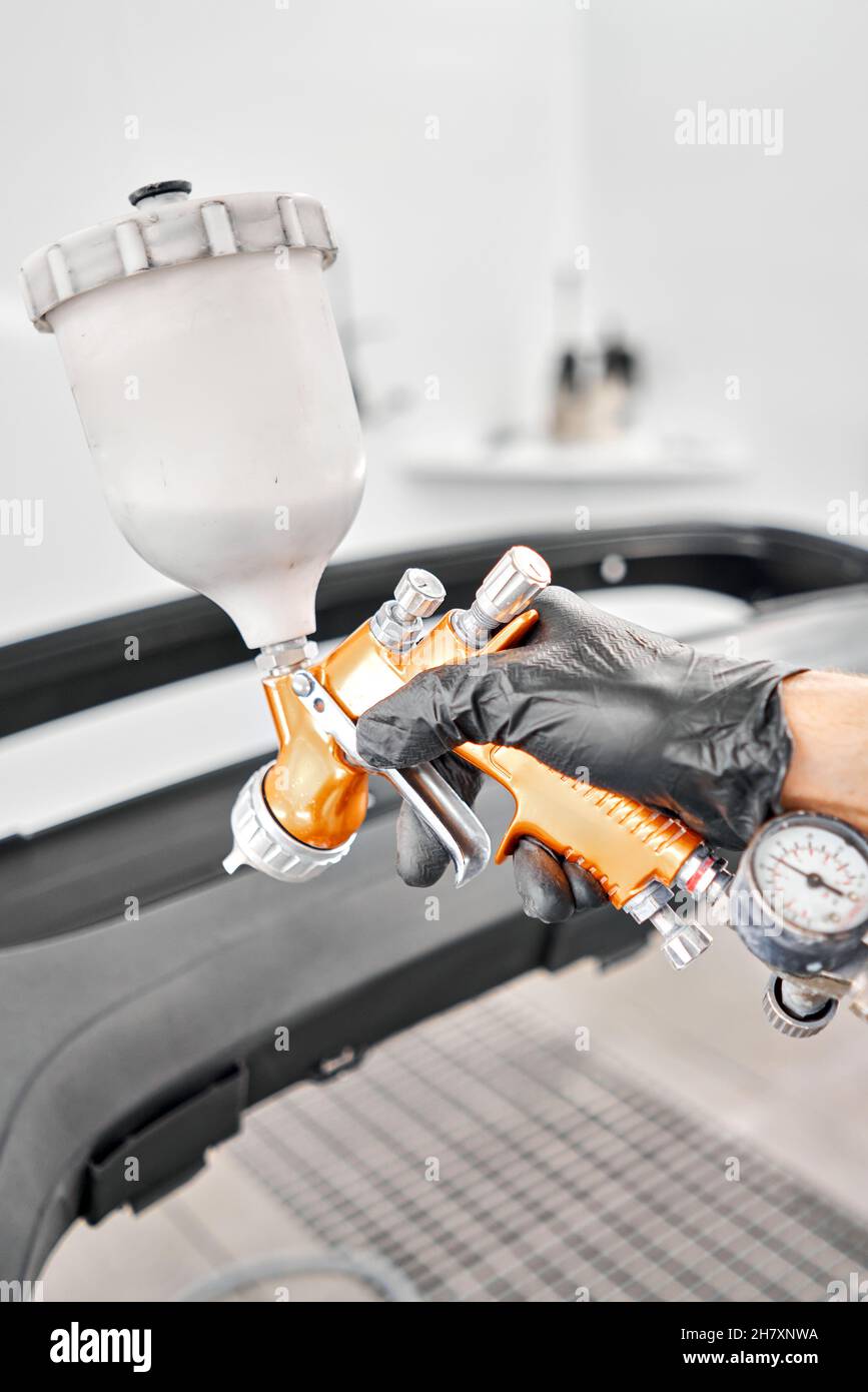 Worker painting parts of the car in special painting chamber, wearing ...