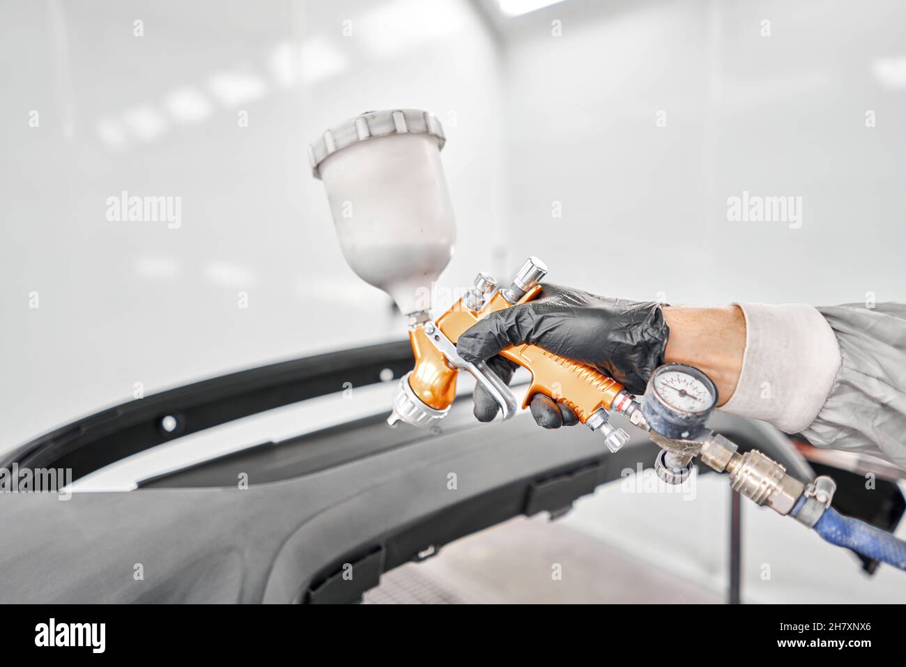 Worker painting parts of the car in special painting chamber, wearing ...