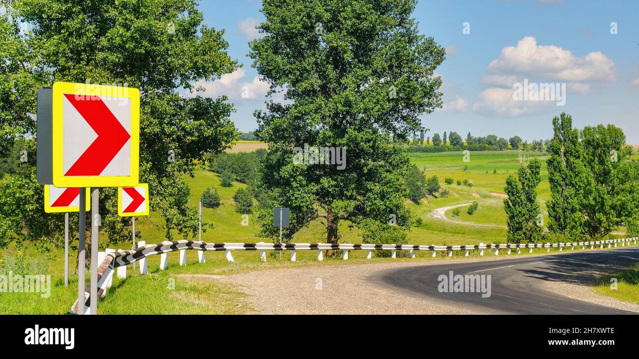 A winding road with steep turns in the hilly terrain. Warning signs ...