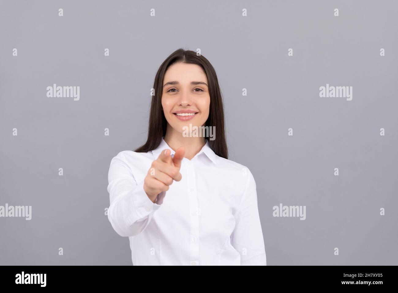 smiling businesslike woman in white shirt pointing finger on grey ...