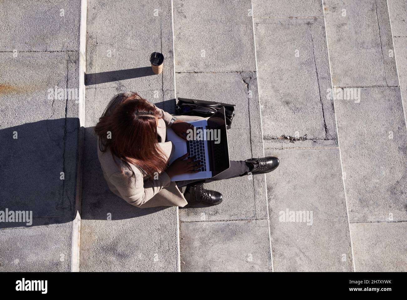 Top view of a young woman sitting on a ladder with a laptop computer ...