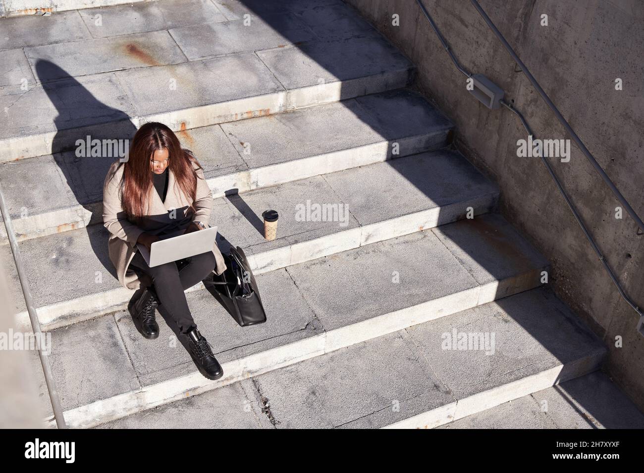 Top view of a young woman sitting on a ladder with a laptop computer ...