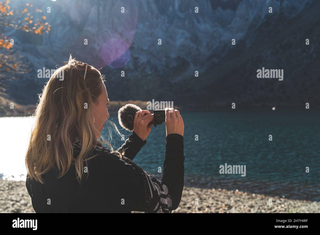 Female travel influencer filming with video camera in front of mountain ...