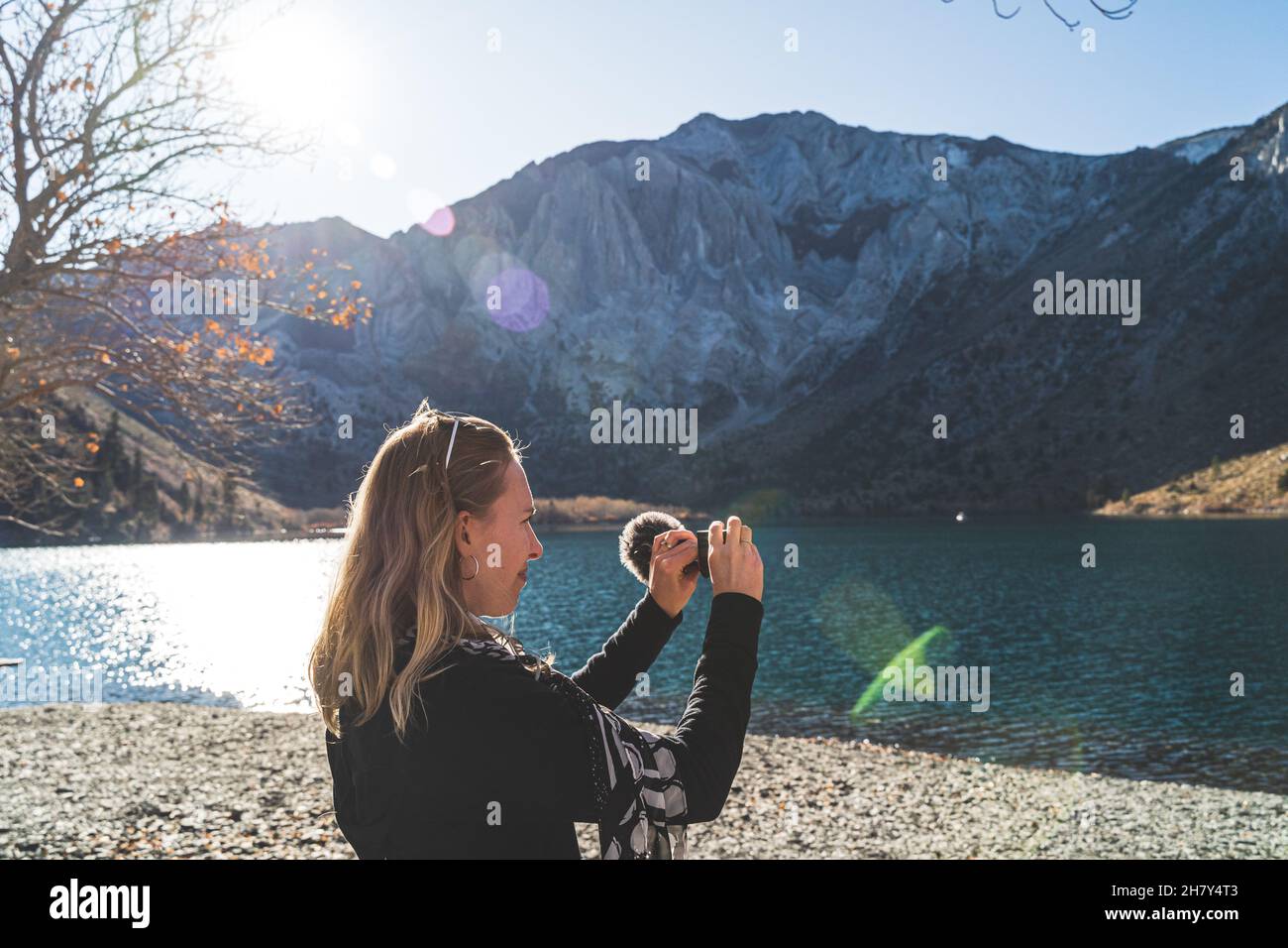Female travel influencer filming with video camera in front of mountain ...