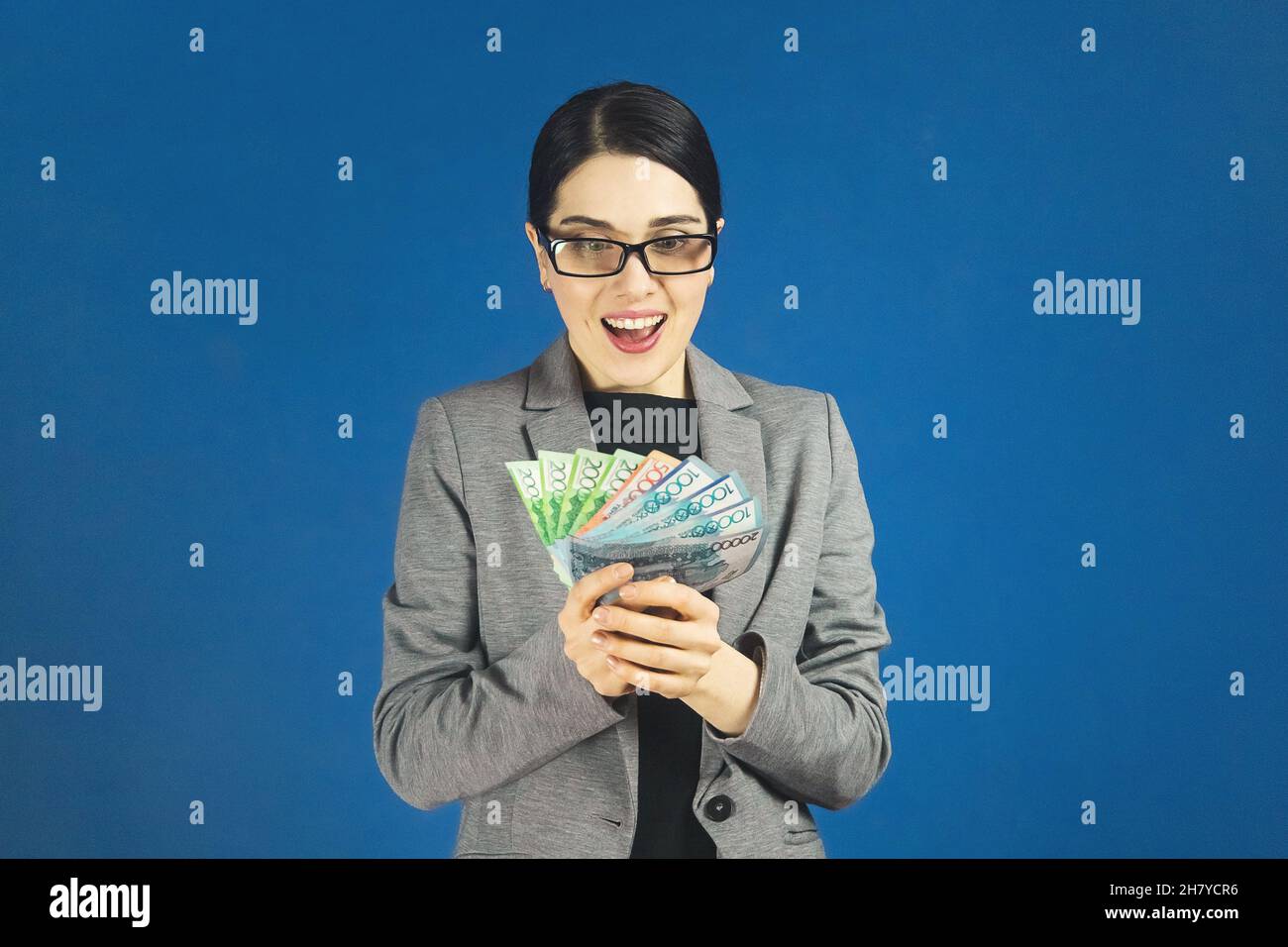 Happy young woman in glasses looks at a pack of tenge with interest on ...