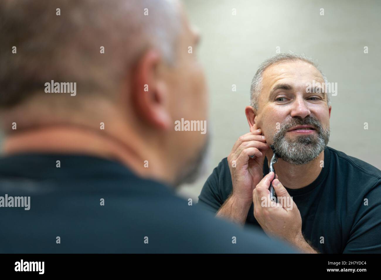 Charming middle aged man shaving his beard and moustache off in front ...