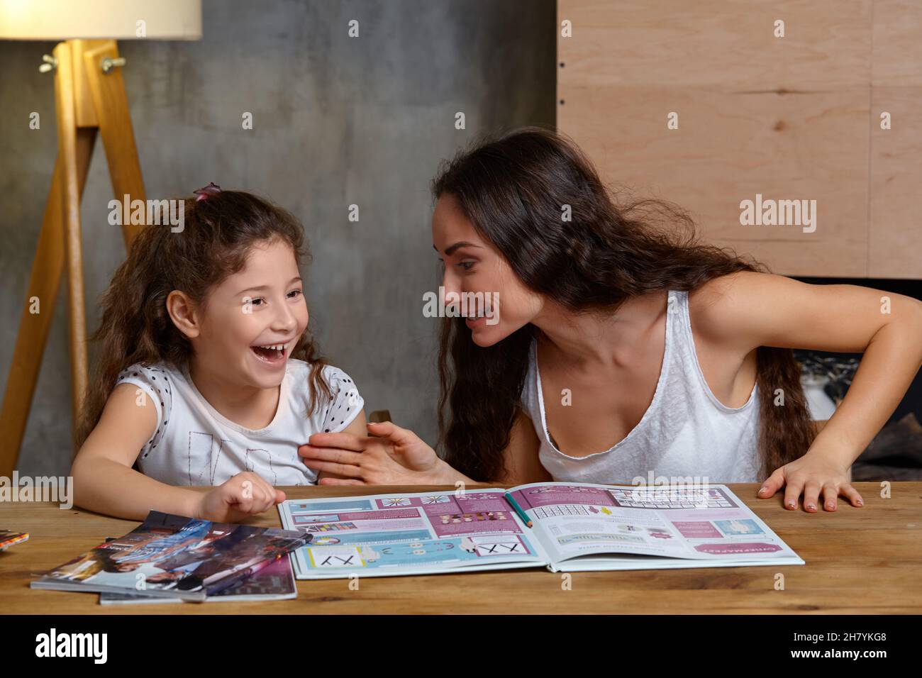 Portrait of a mother helping her small sweet and cute daughter to make her homework indoors ...
