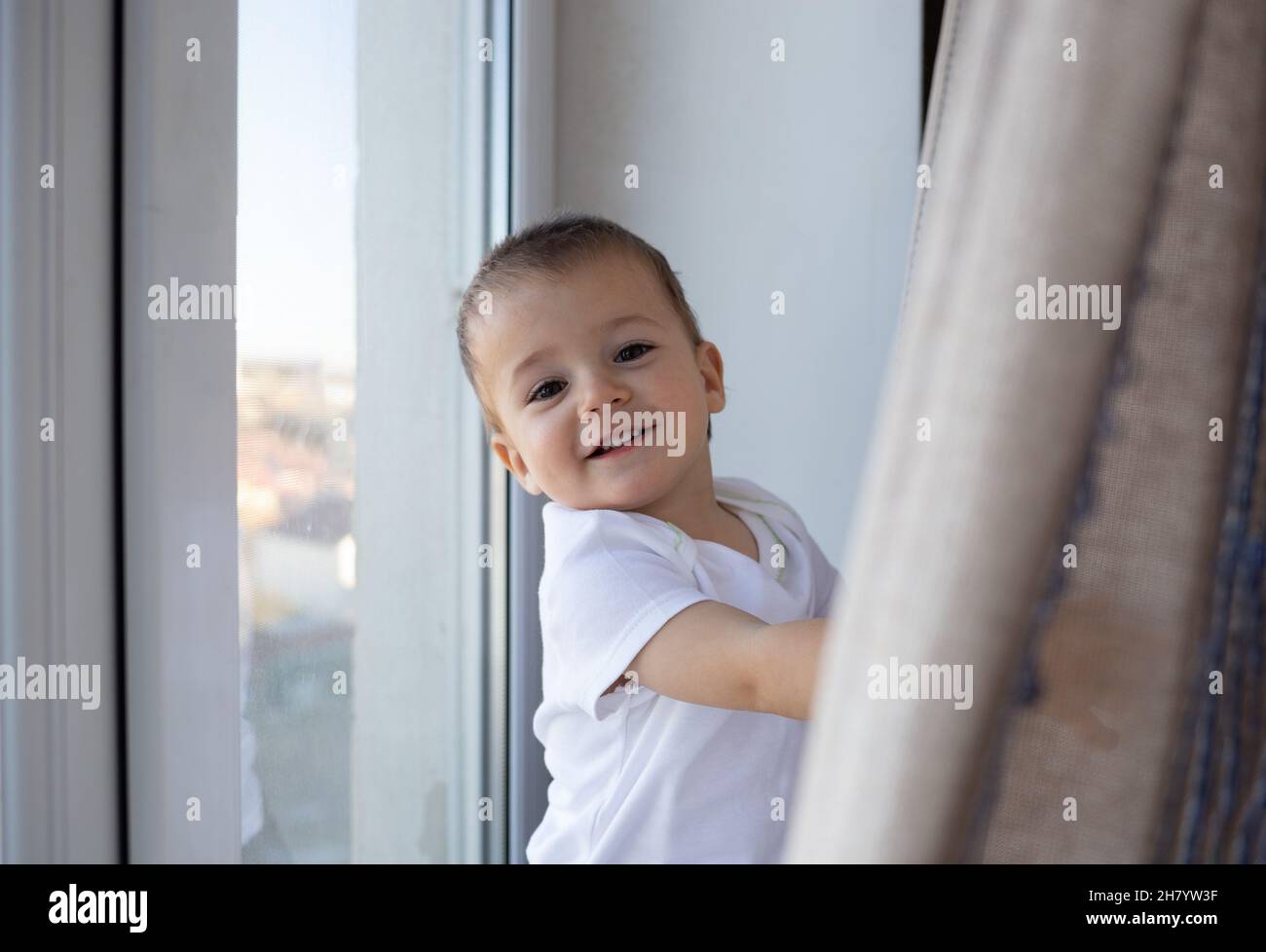 little boy smiling standing on the windowsill by the window behind the ...