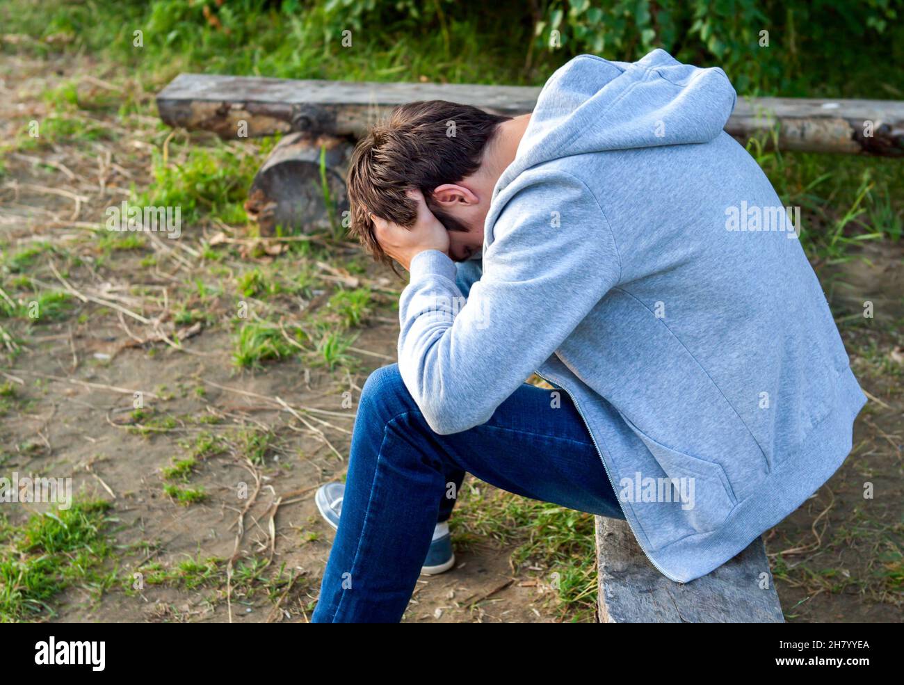 Sad Young Man sit on the Log outdoor Stock Photo - Alamy