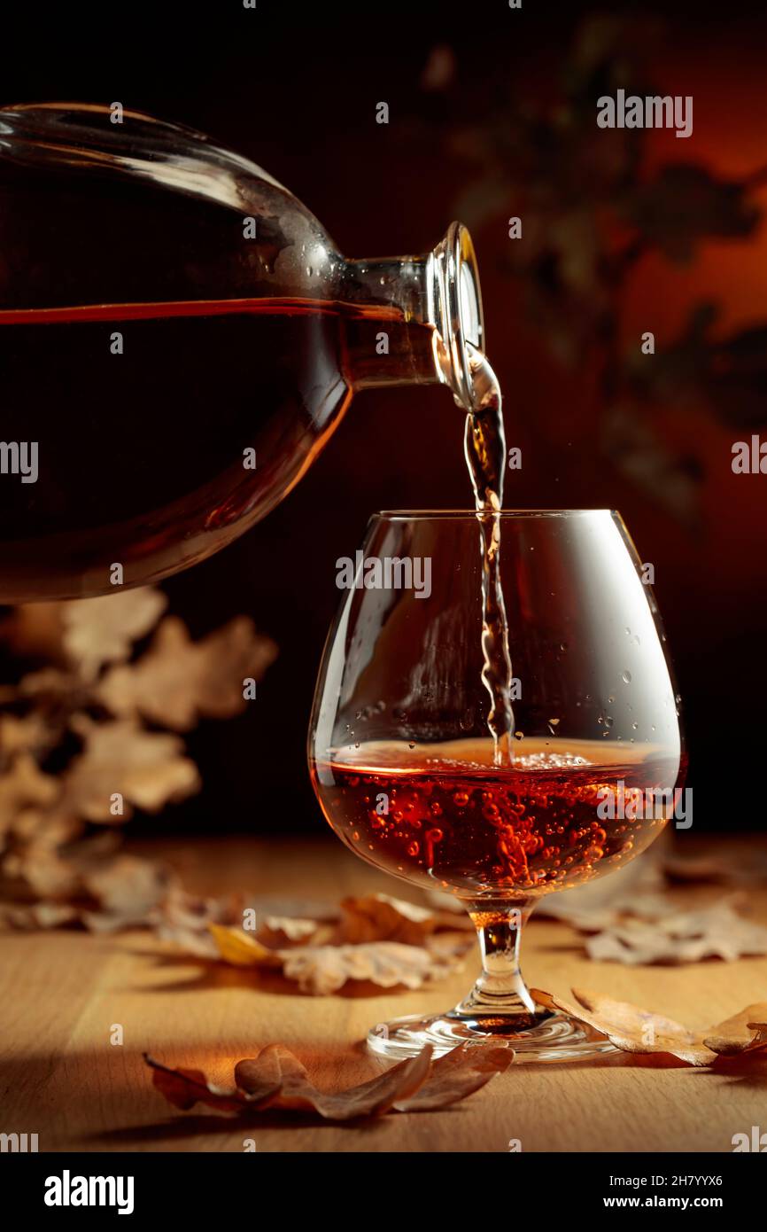 Cognac is poured into a glass from a bottle. A snifter of brandy on an ...