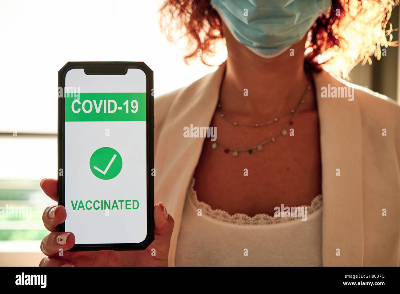 a woman with protective mask showing covid-19 vaccination certificate ...