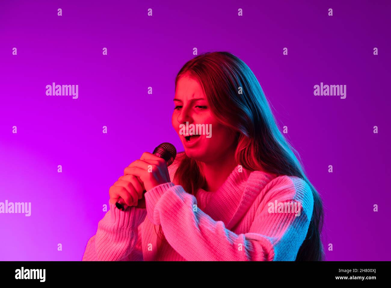 Young smiling beautiful girl singing with microphone isolated on purple ...