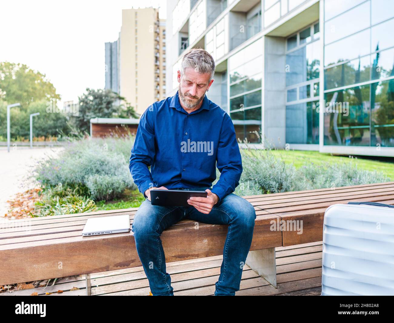 Positive adult male entrepreneur working on tablet on wooden bench near ...