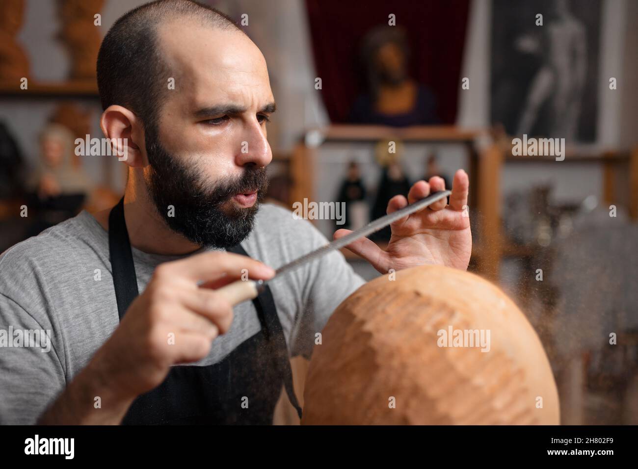 Concentrated bearded male master in apron using rasp to shape round ...