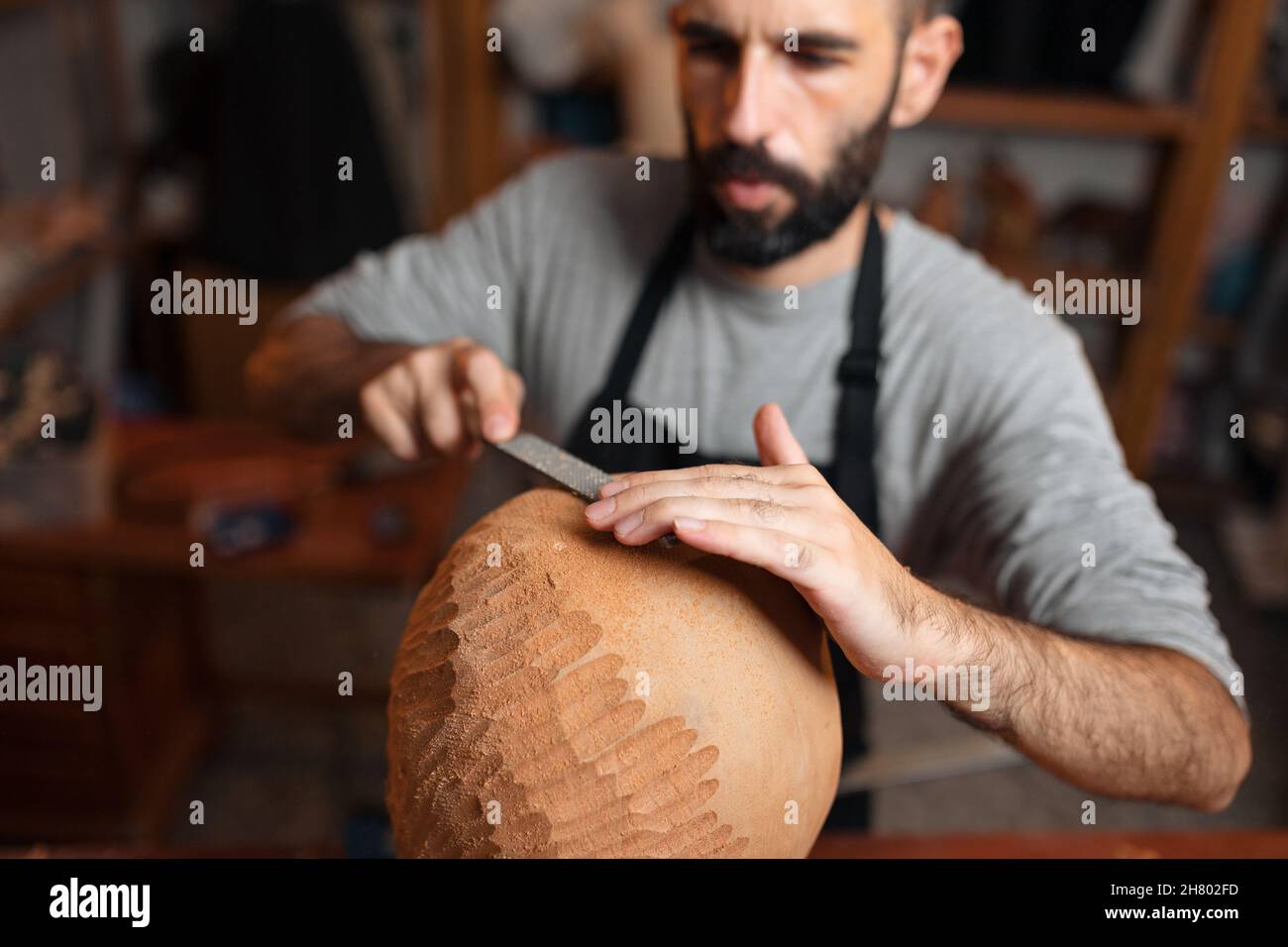 Concentrated bearded male master in apron using rasp to shape round ...