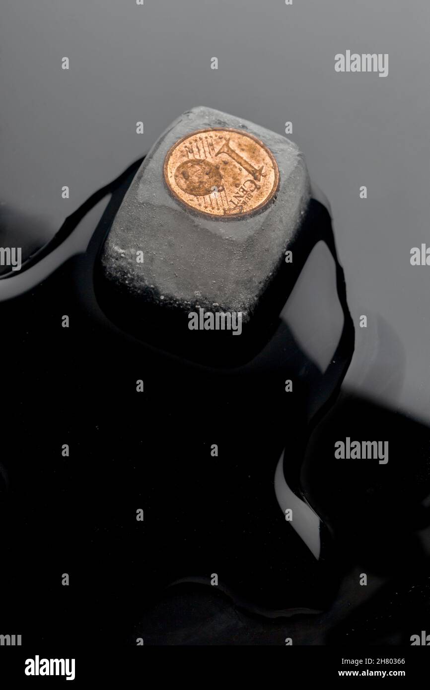 From above of cold translucent ice cube with golden coin melting on wet ...