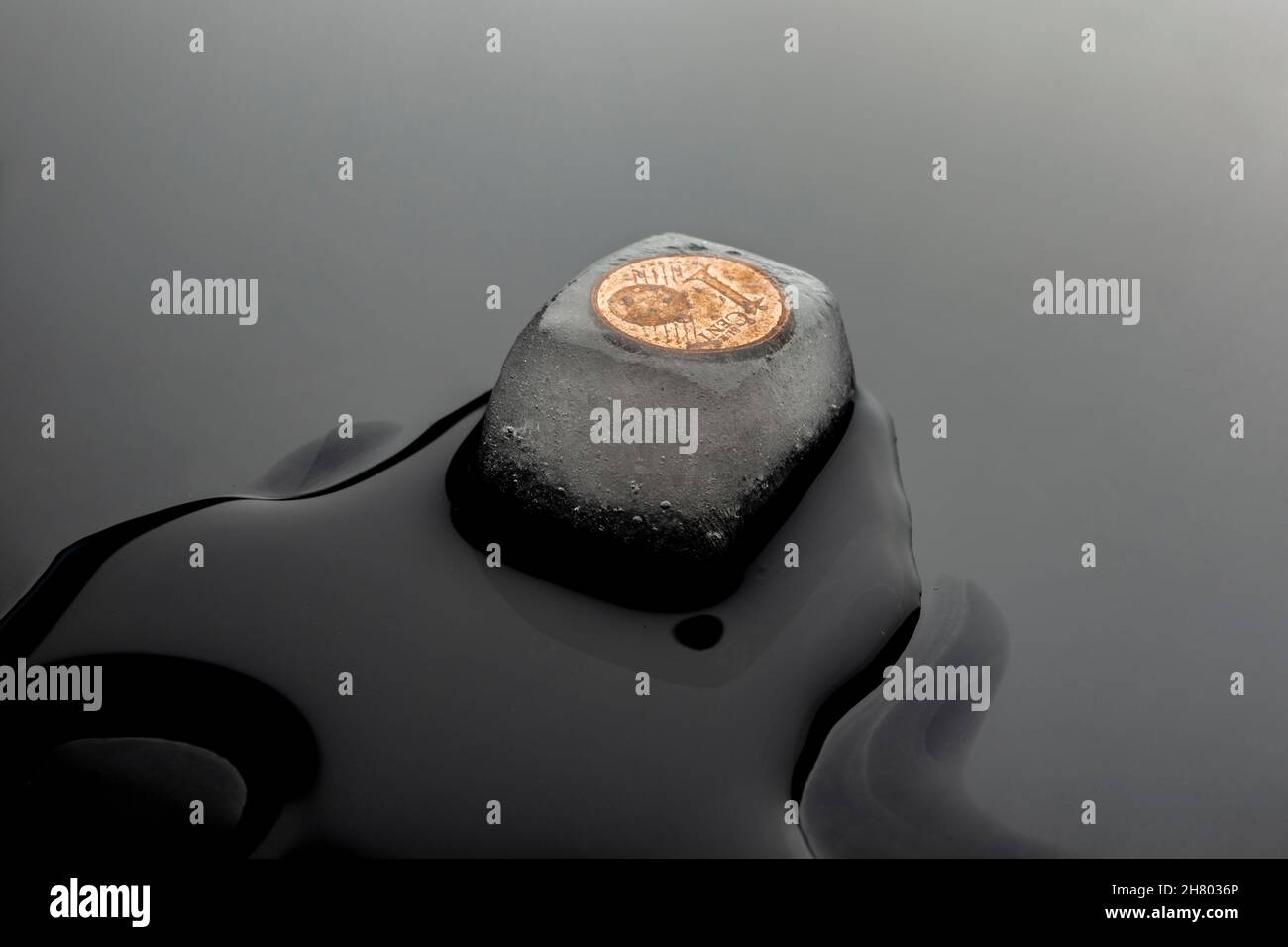 From above of cold translucent ice cube with golden coin melting on wet ...