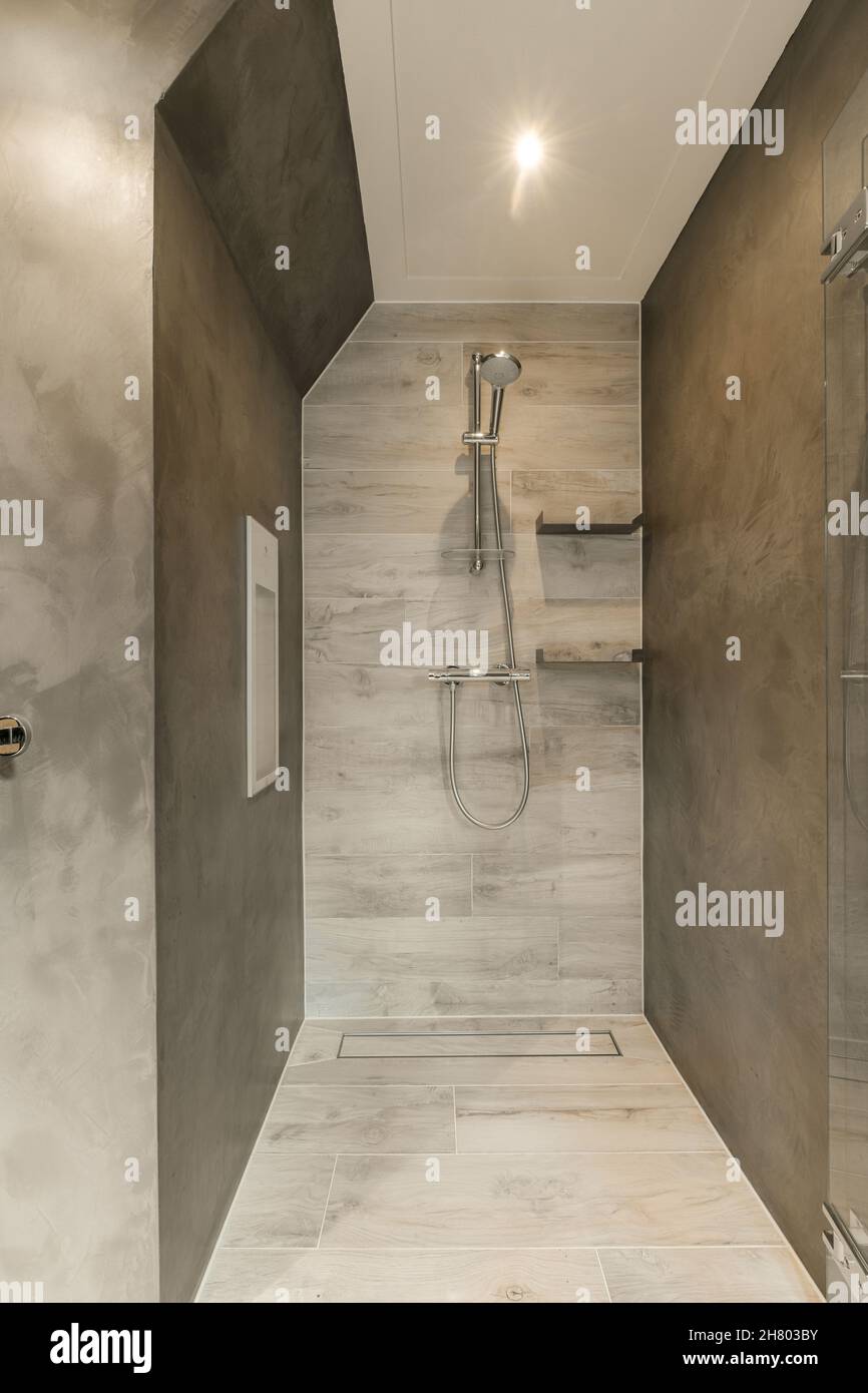 Shower set in empty narrow space with gray walls and floor under lamp ...