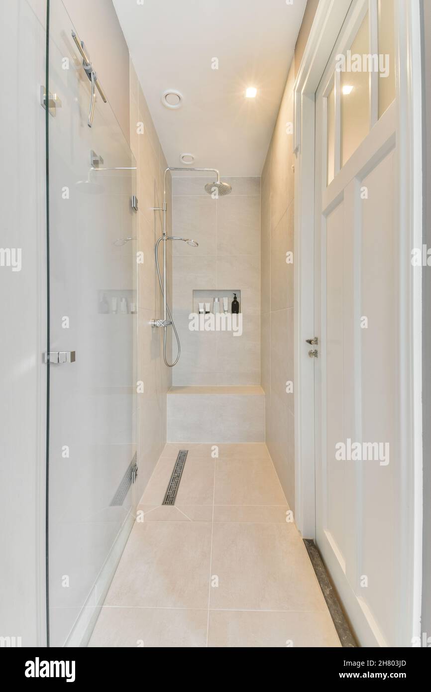 Empty narrow shower with light tiled walls and glass door in modern ...