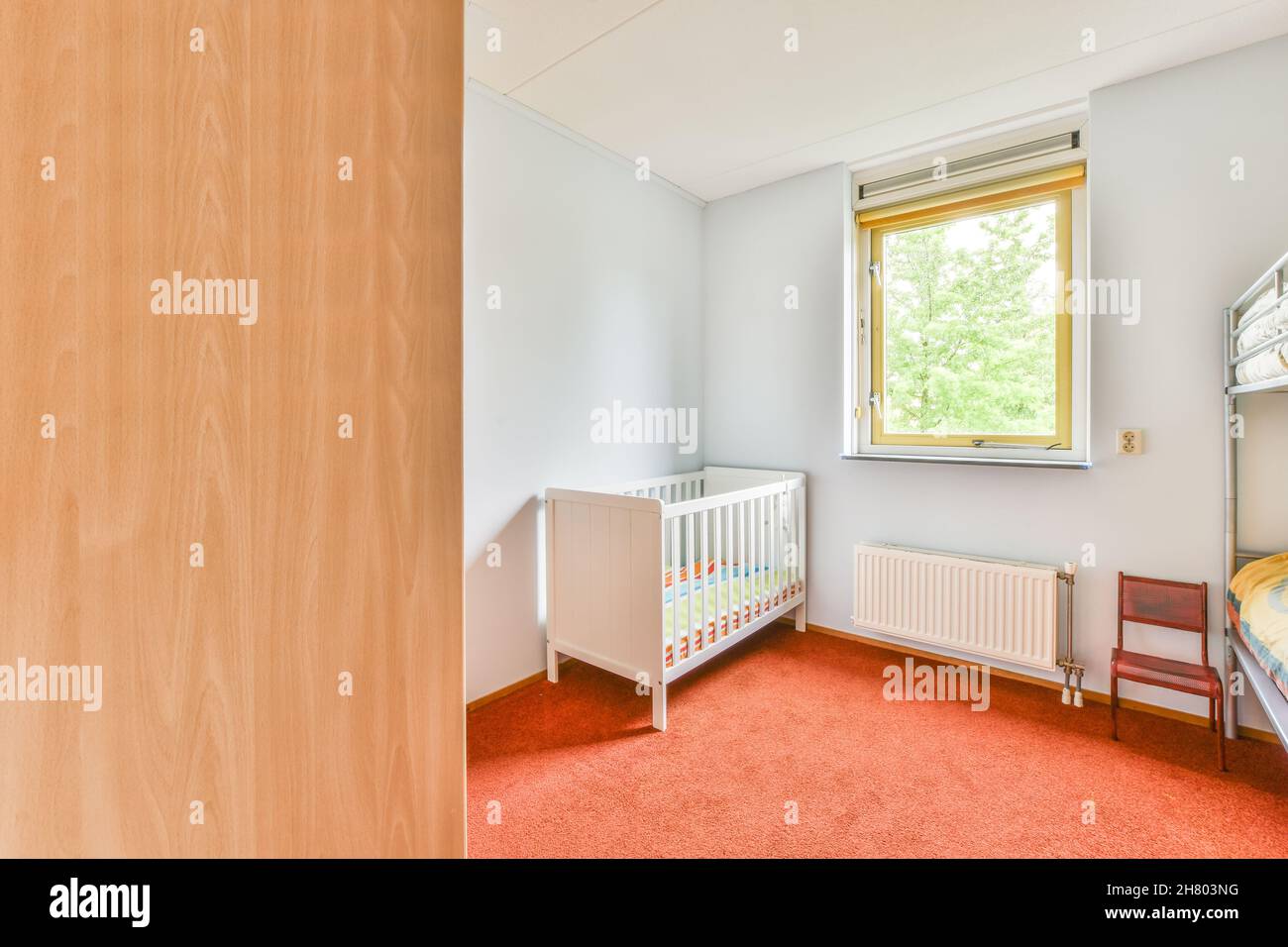 Bunk bed with blankets and pillows placed at wall against white crib in ...