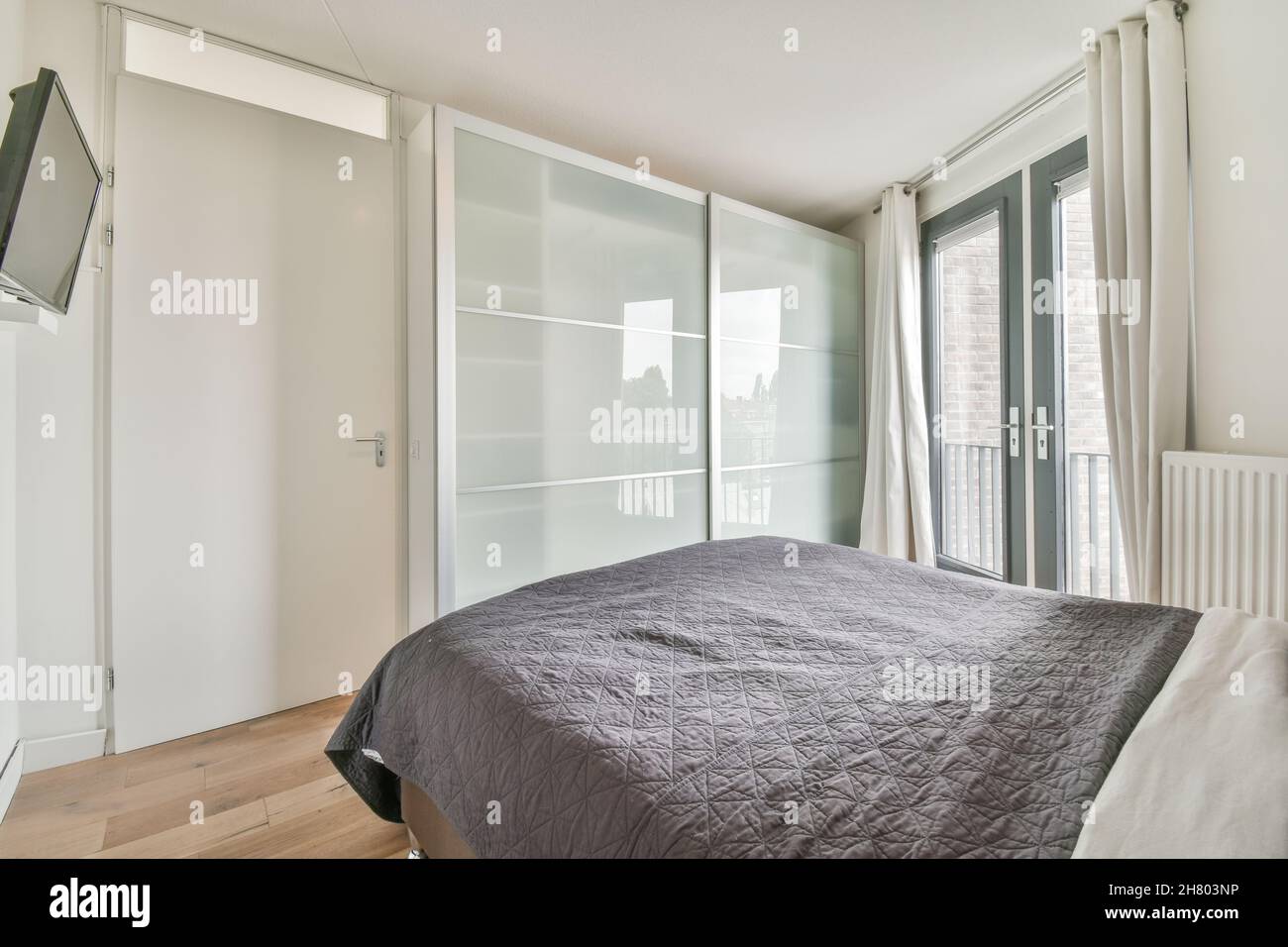 Comfortable bed with blanket placed near TV in light spacious bedroom ...