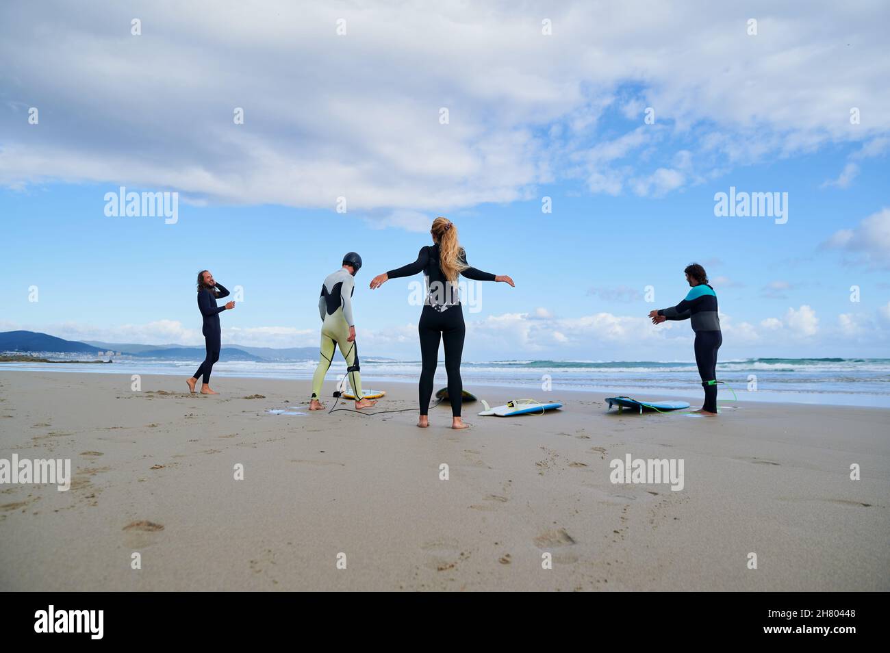 Full body of male and female surfers doing warming up exercises on wet ...