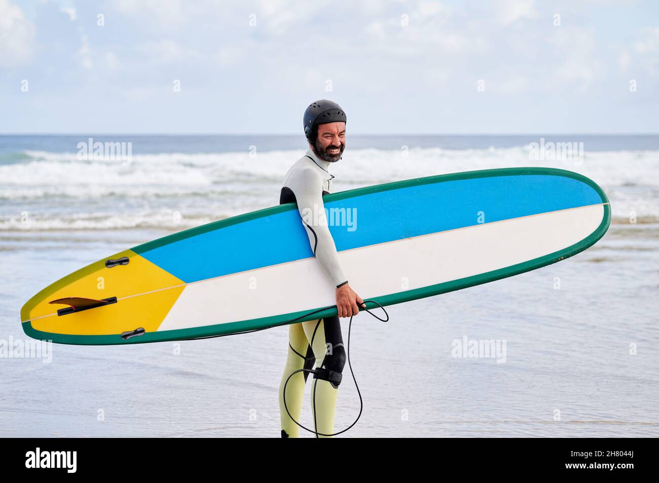 Back view of male surfer in wetsuit and helmet carrying surfboard ...