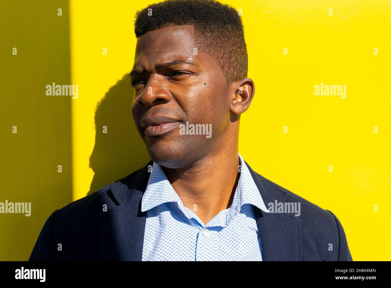 African American male in formal wear frowning face from sunshine while ...