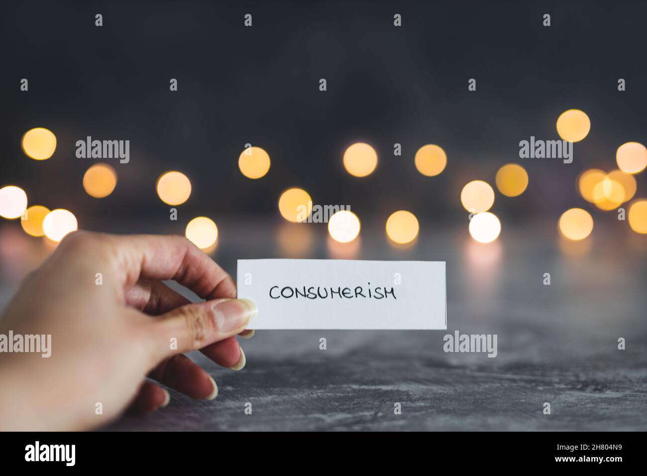hand holding label with Consumerism text in front of shiny fairy lights ...