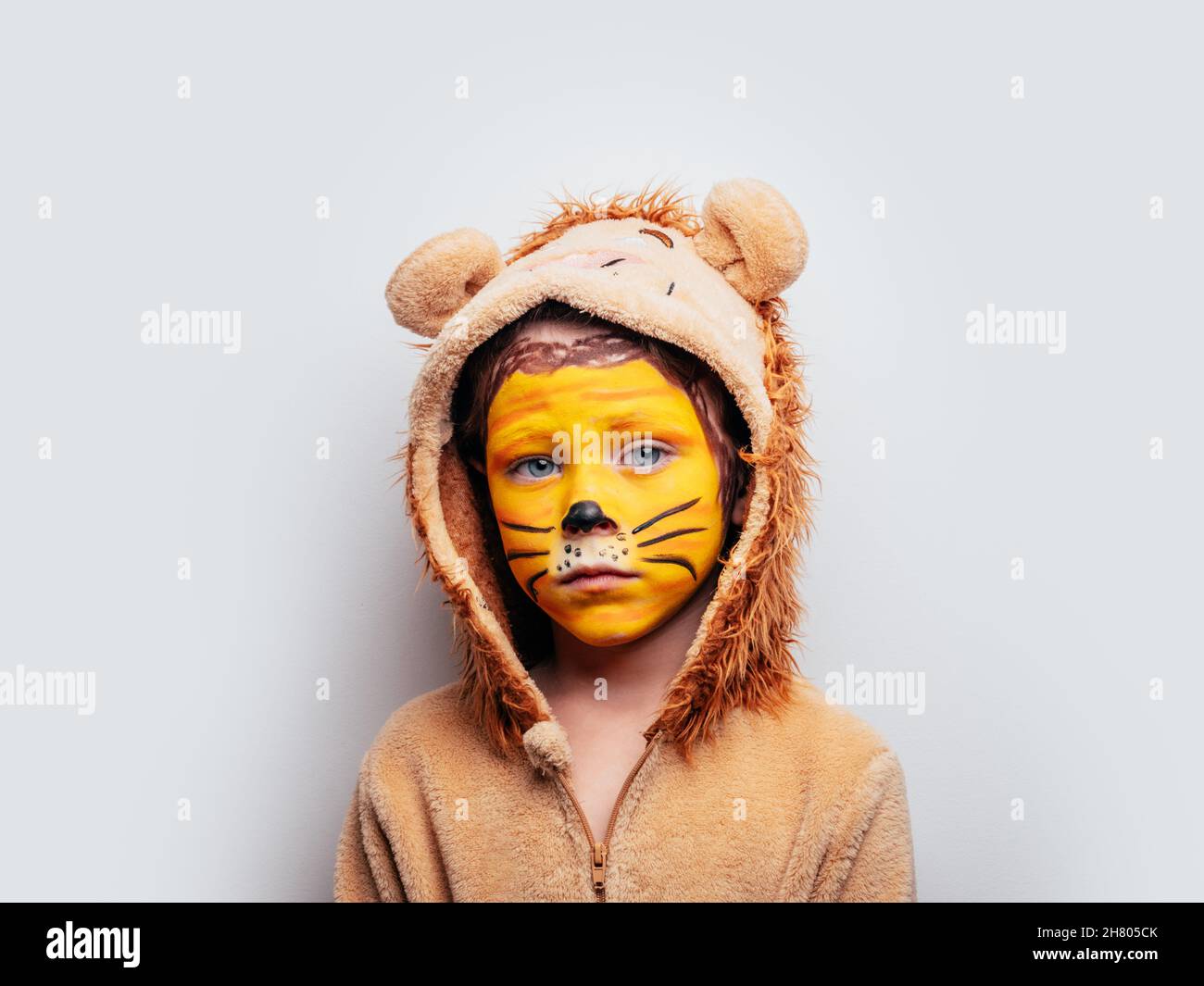 Sad boy in lion outfit with painted face wearing hood with mane looking ...