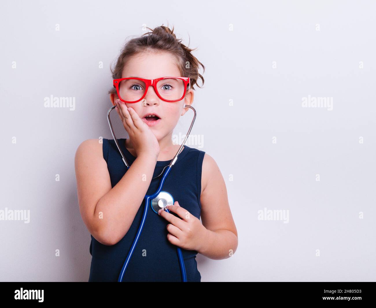 Amazed girl in doctor costume with glasses listening to heartbeat with ...