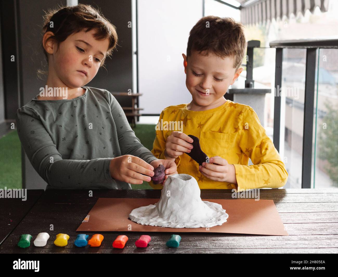 Attentive little boy molding crater of handmade plasticine volcano ...
