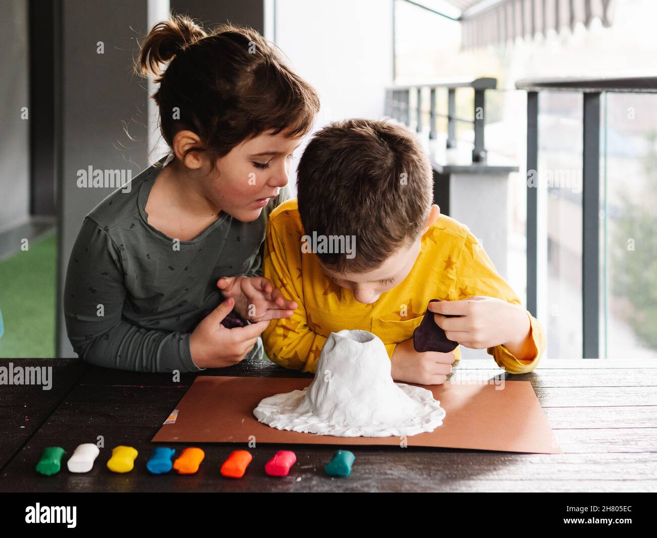 Attentive little boy looking into crater of handmade plasticine volcano ...