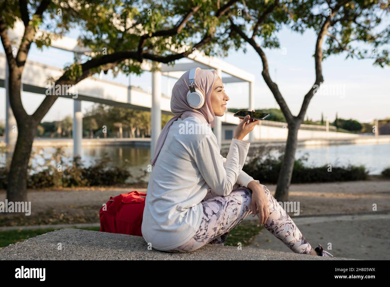 Positive Arab female in hijab sitting on stone staircase near backpack ...