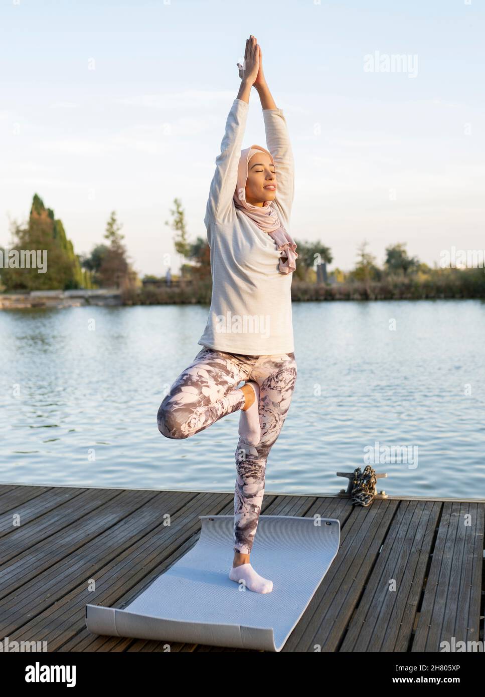Full body of tranquil Arab female in hijab doing Tree with arms up ...