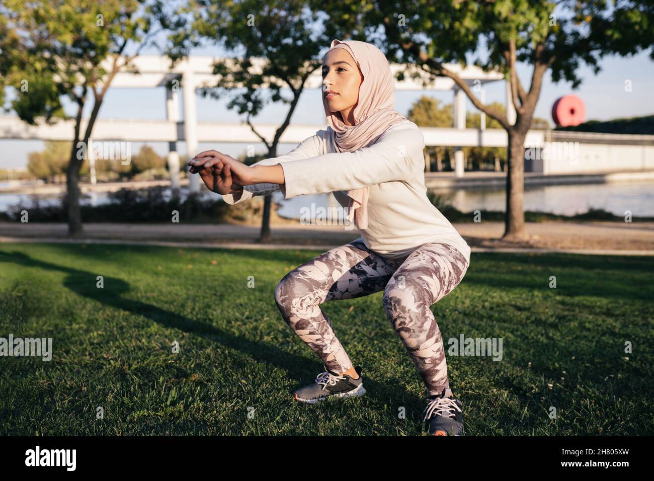 Full body of determined Muslim female in hijab doing squat extending ...