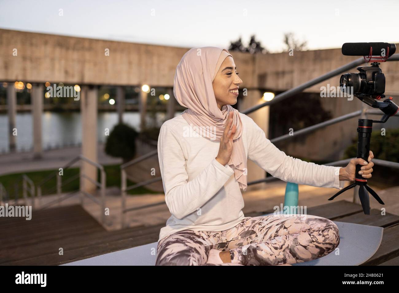 Happy Arab female blogger in hijab waving hand while shooting video on ...