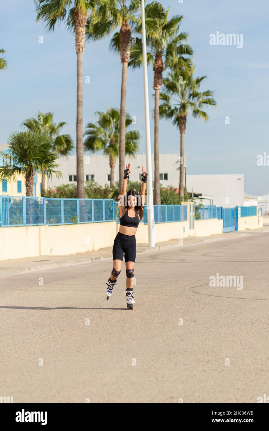 Full body of happy fit female in sportswear roller blading with hands ...